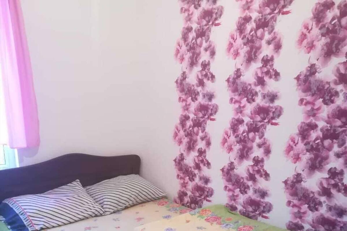 Quarto com cama, travesseiros, edredom verde e papel de parede floral.