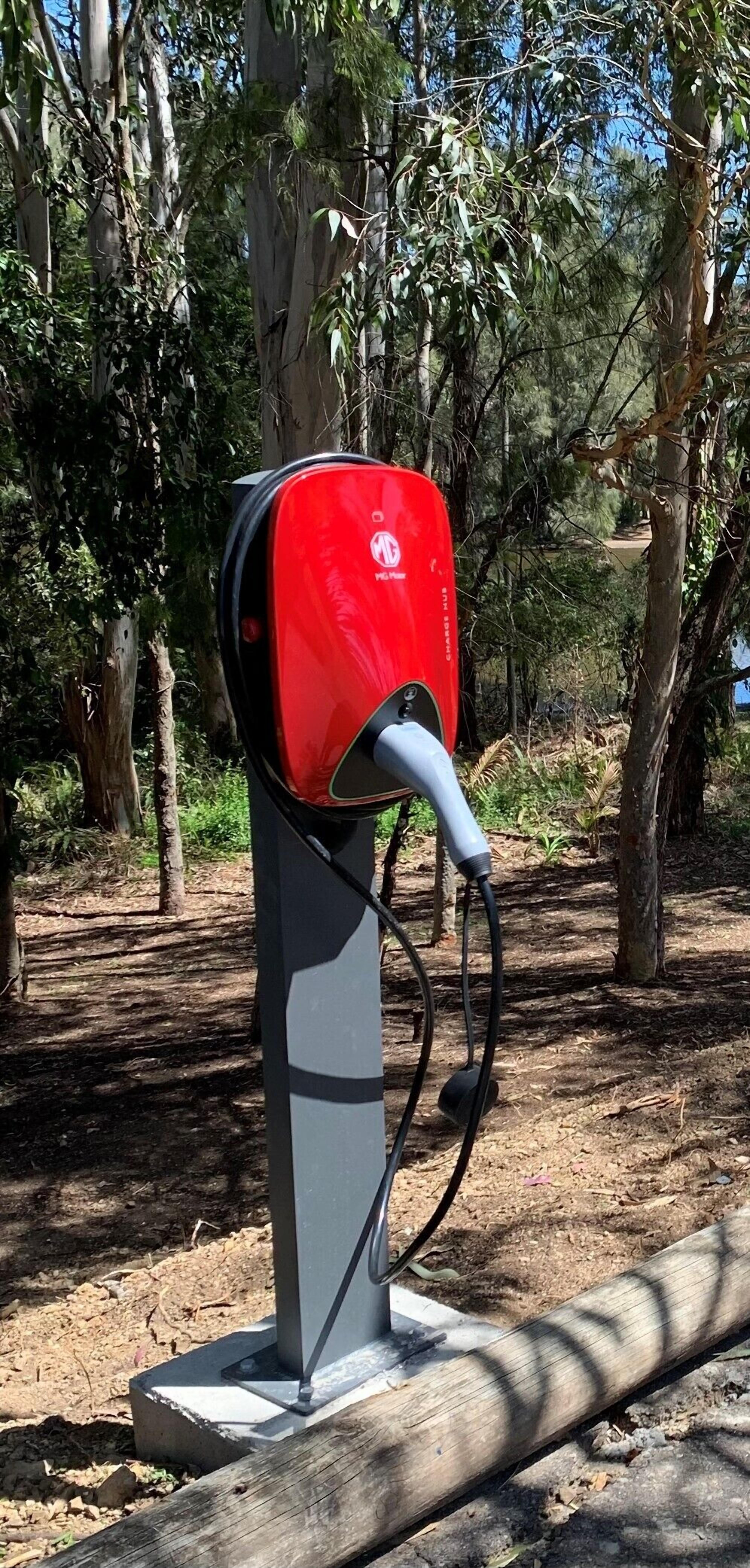 Estação de carregamento para veículo elétrico vermelha numa área arborizada.