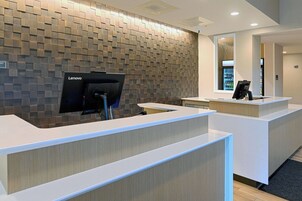 Uma área de recepção moderna com um posto de computador Lenovo, uma geladeira e um espelho.