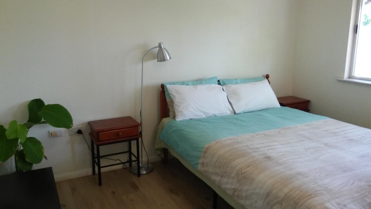 Quarto com uma cama, mesa de cabeceira, abajur e planta em vaso.