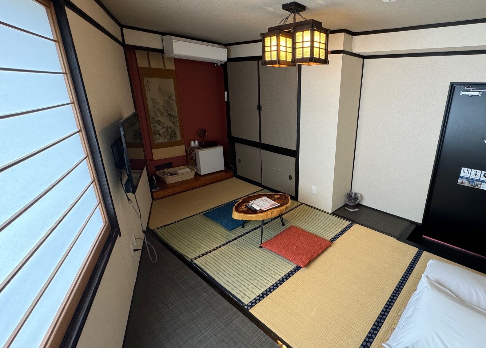 Um quarto japonês tradicional com tatames, uma mesa baixa com um menu, um pequeno aquecedor e uma televisão na parede.