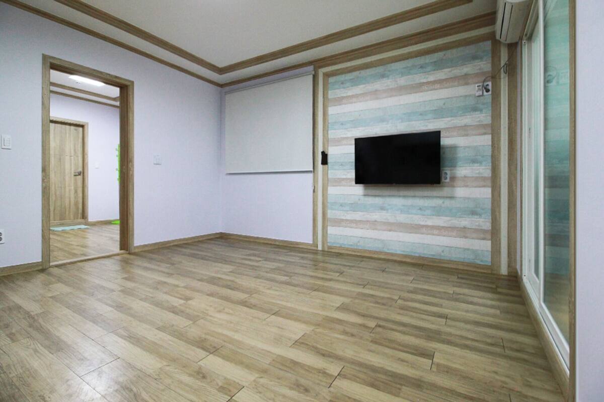 Quarto com piso de madeira, televisão montada, porta de vidro deslizante e porta de madeira que dá para outro cômodo.