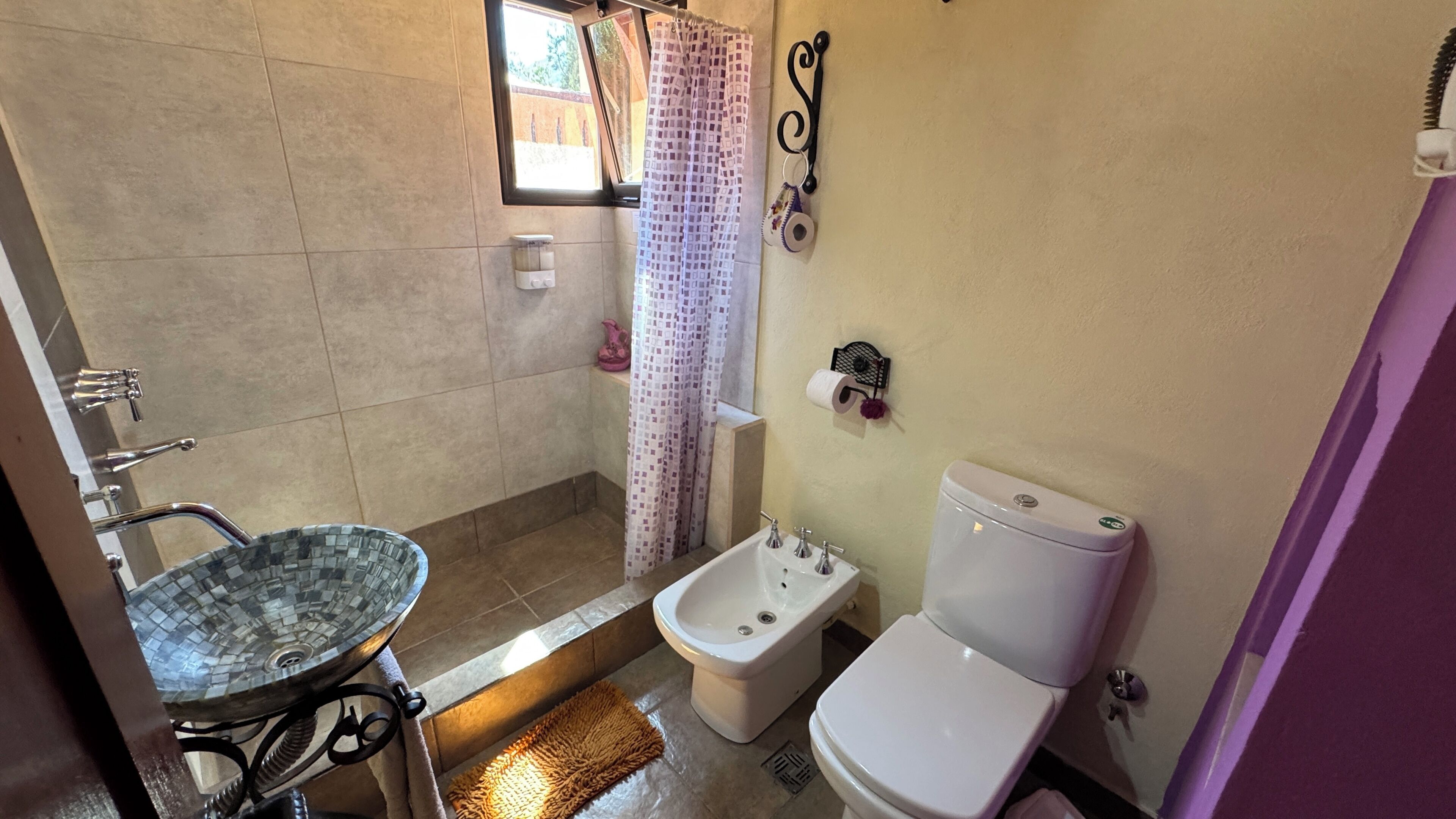 Casa de banho com lavatório em mosaico, bidé, sanita e cortina de chuveiro.