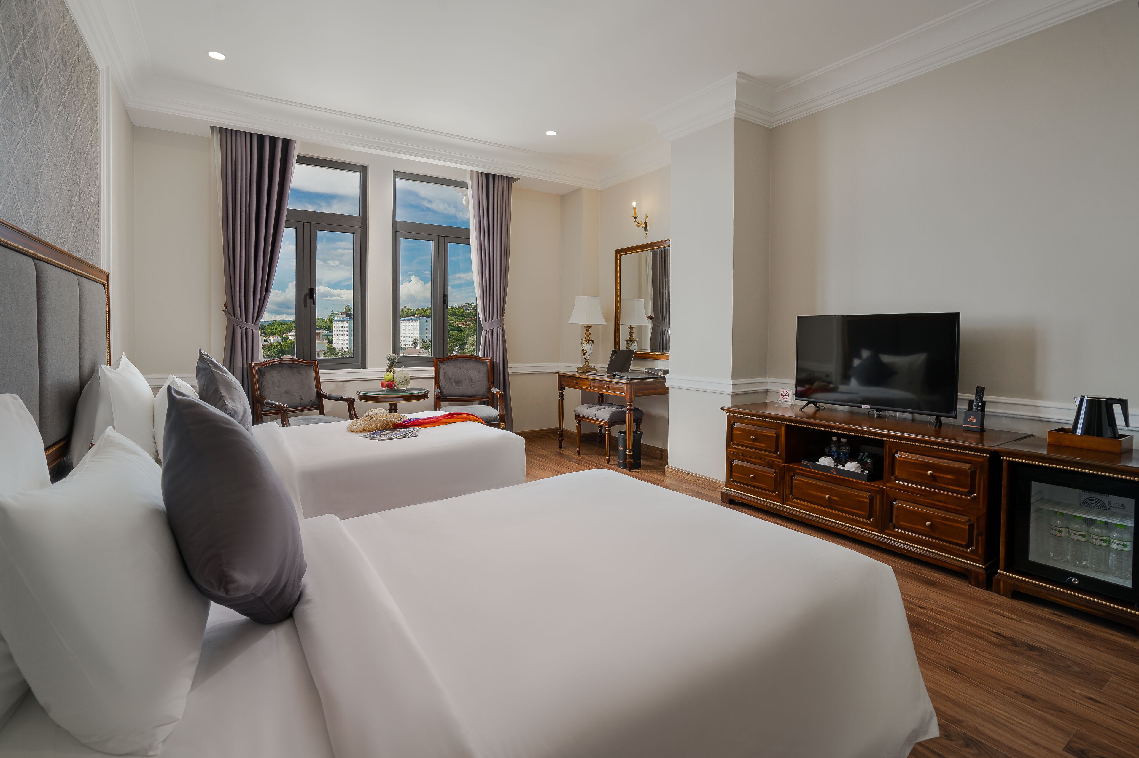 Quarto de hotel com duas camas, uma escrivaninha, televisão e minibar.