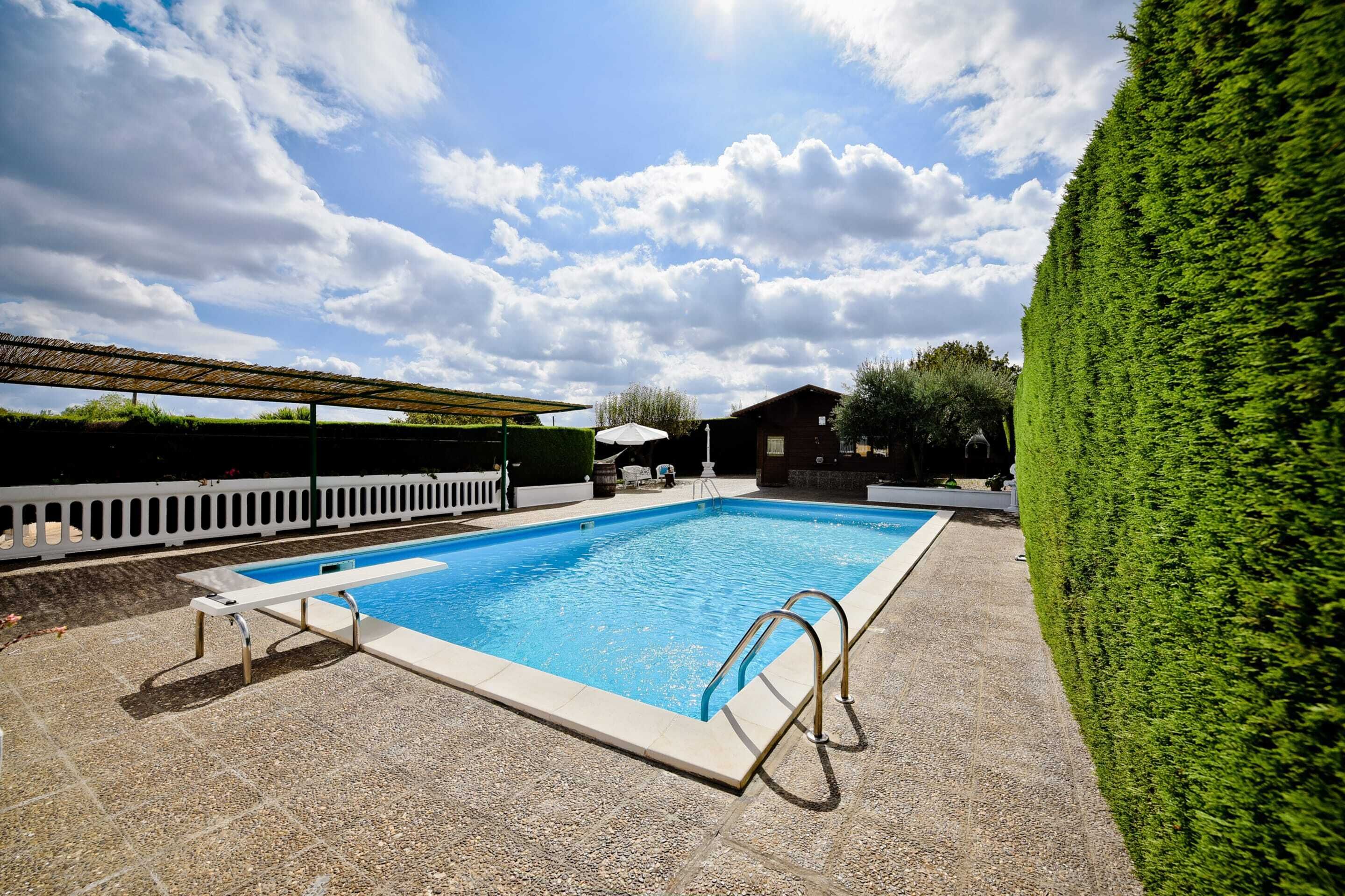 Uma piscina retangular com escada de metal e um deck branco.