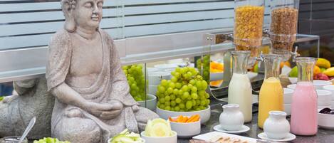 Uma estátua de Buda cercada por um buffet com frutas, legumes e bebidas variadas.