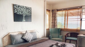 Quarto com cama, cadeira, escrivaninha e janela com cortinas.