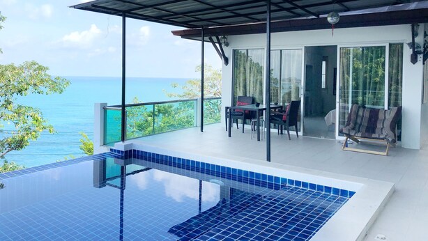Uma piscina infinita moderna com vista desobstruída para o oceano, área externa coberta com mesa e cadeiras, e uma grande porta de vidro deslizante que dá acesso a um espaço privativo.