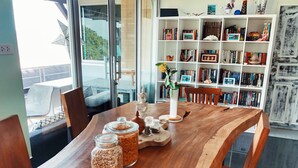 Uma mesa de jantar de madeira com potes de vidro, um vaso com flores e uma estante repleta de livros e objetos decorativos.