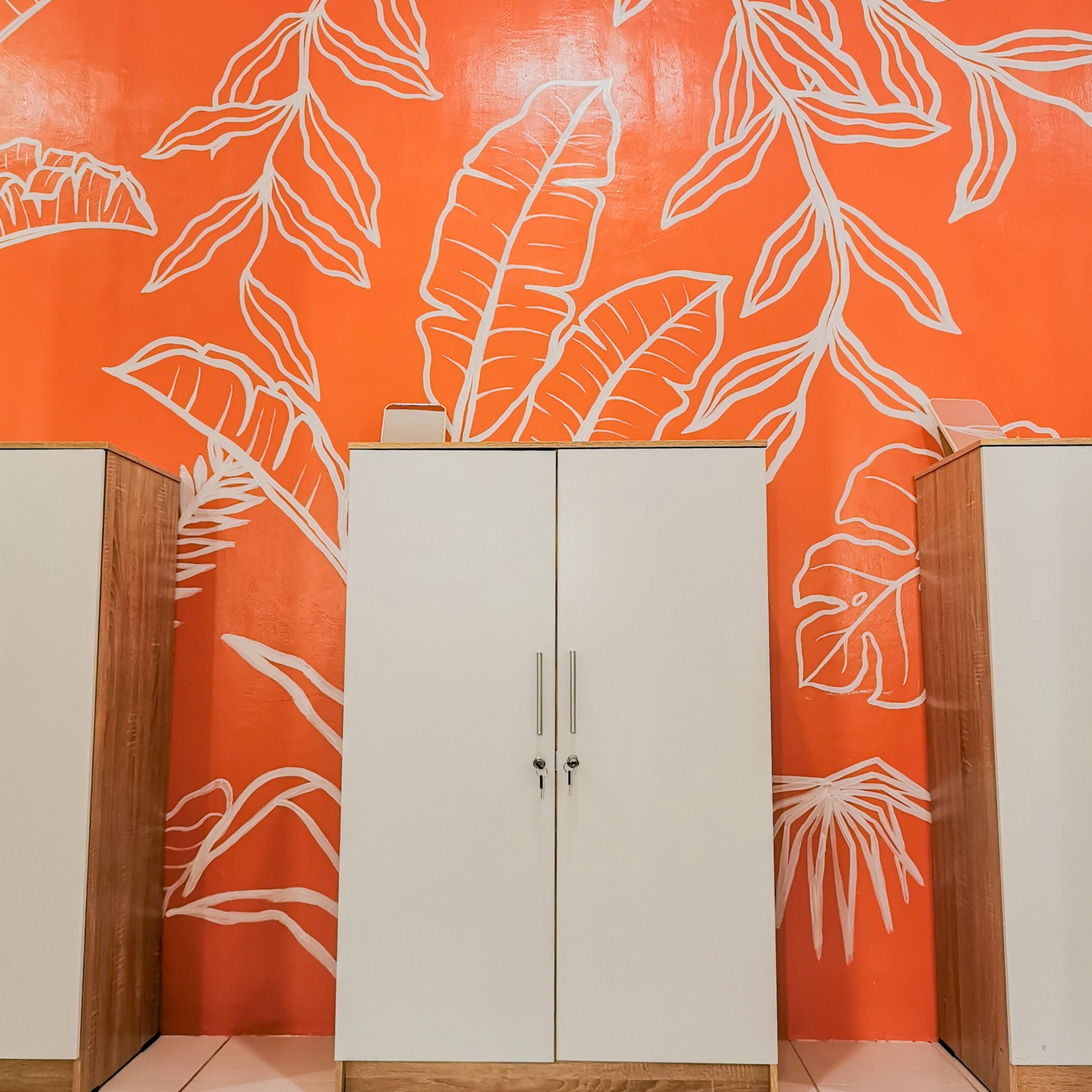 Quarto com um guarda-roupa branco em frente a uma parede laranja com motivos de folhas brancas.