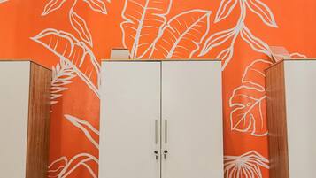 Quarto com um guarda-roupa branco em frente a uma parede laranja com motivos de folhas brancas.