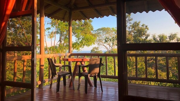 Um deck de madeira com mesa e cadeiras, com vista para uma paisagem natural.