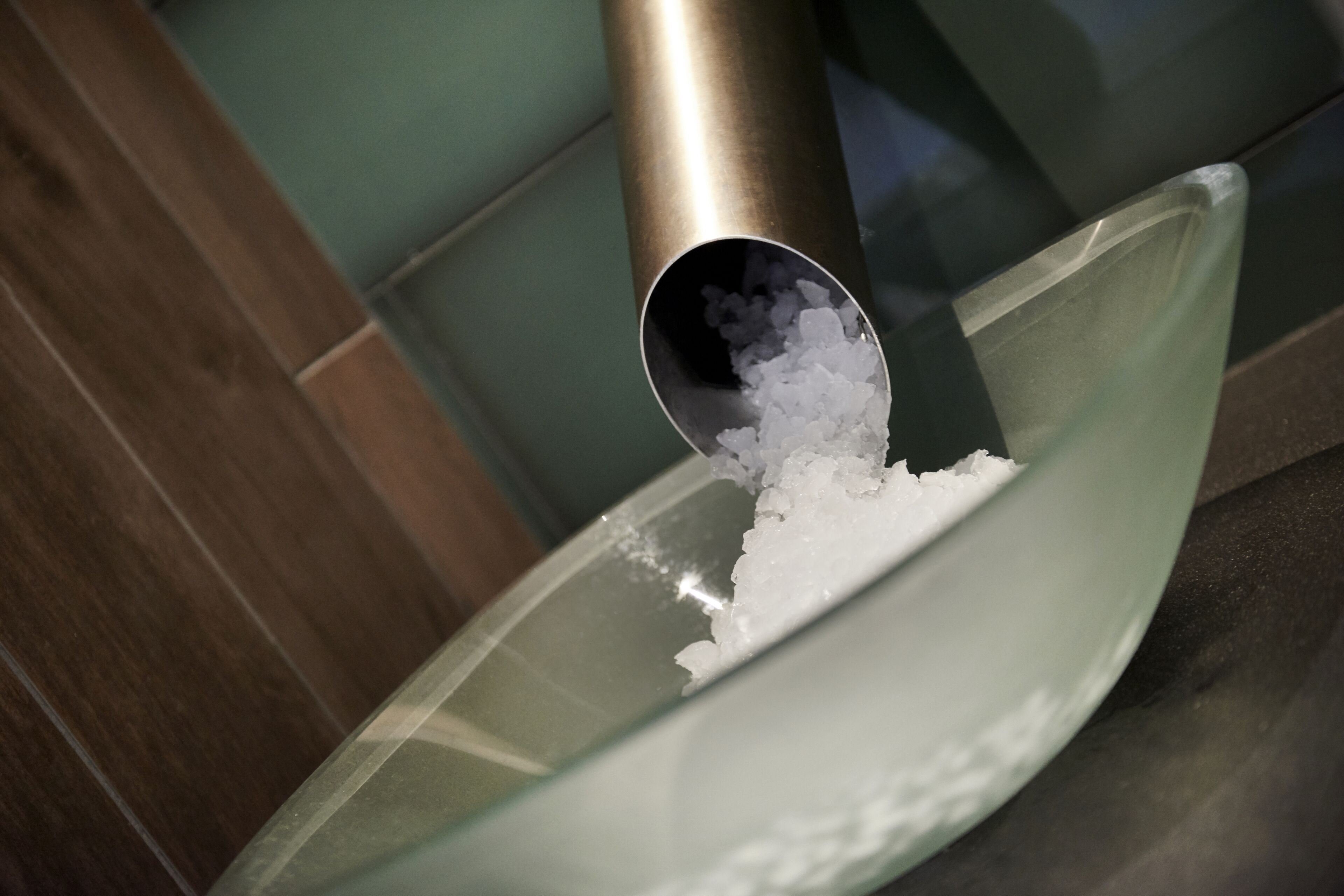 Uma colher de sal sendo despejada em uma tigela de vidro.