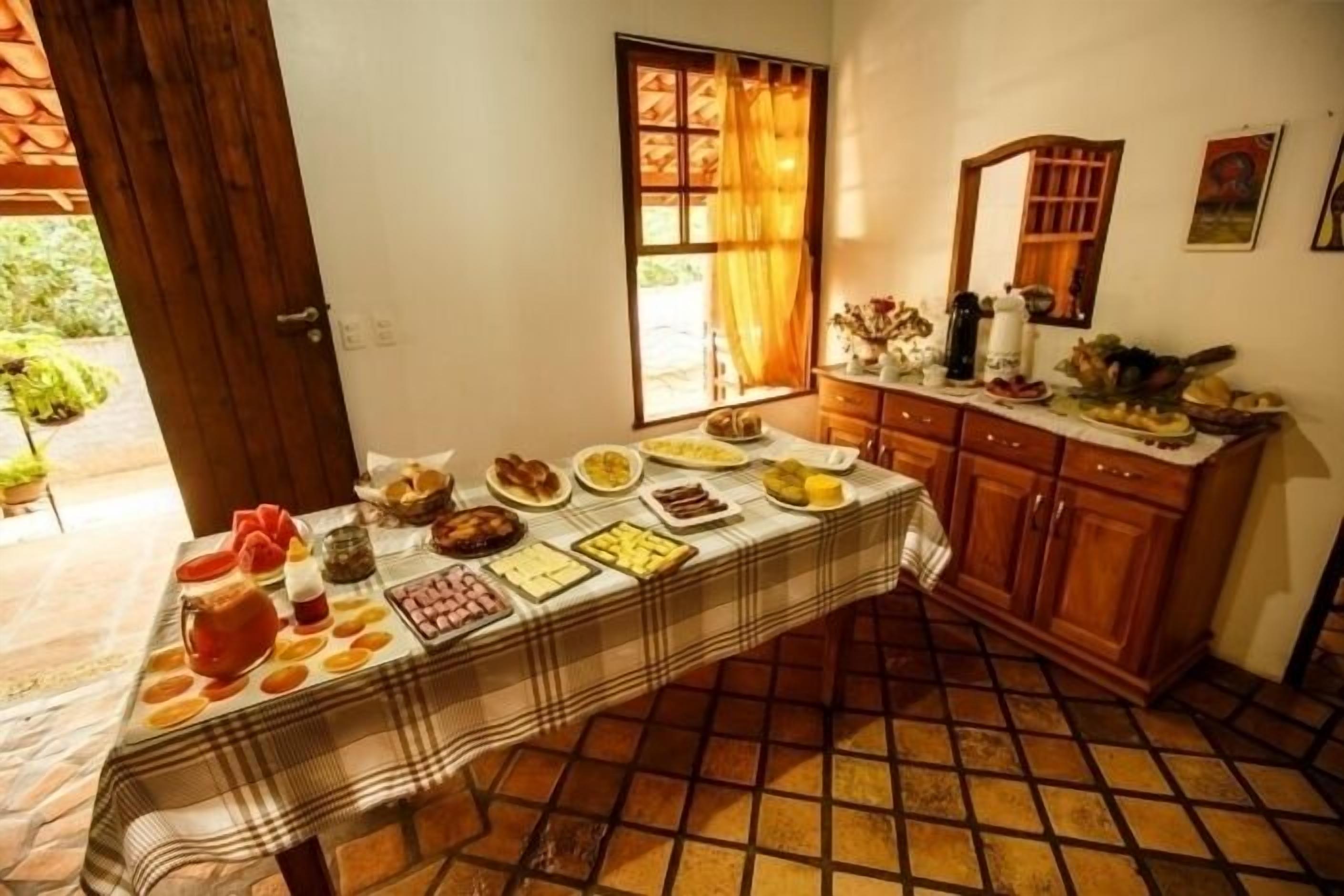 Uma sala de jantar com uma mesa posta para refeição, um armário de madeira e uma janela com cortinas.