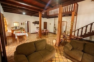 Uma sala de estar acolhedora, com pé direito alto, vigas de madeira, piso ladrilhado e uma escada.