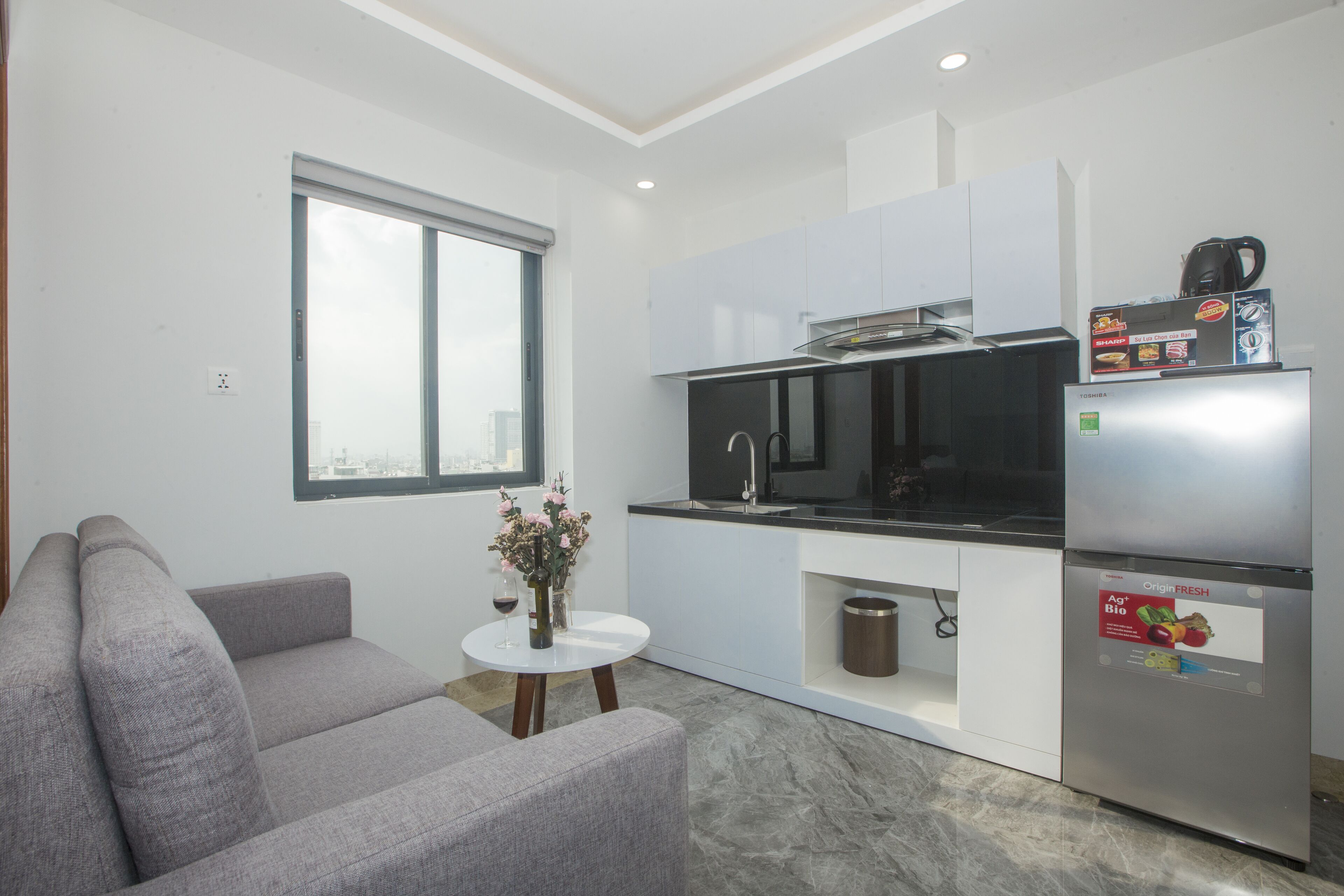 Um espaço de estar compacto com cozinha americana, um sofá, uma pequena mesa com um vaso e uma janela com vista para a cidade.
