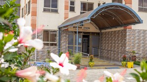 Entrada de hotel com acesso coberto, degraus até a porta e placa indicando serviços como hospedagem, restaurante e piscina.