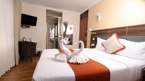 Quarto de hotel com uma cama grande, televisão, escrivaninha e banheiro visível por uma porta aberta.