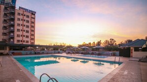 Piscina com vista para um hotel e um pôr do sol.