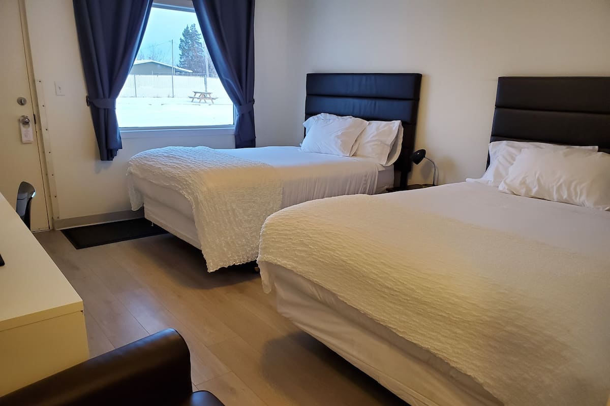 Quarto de hotel com duas camas, uma escrivaninha e uma janela com cortinas.