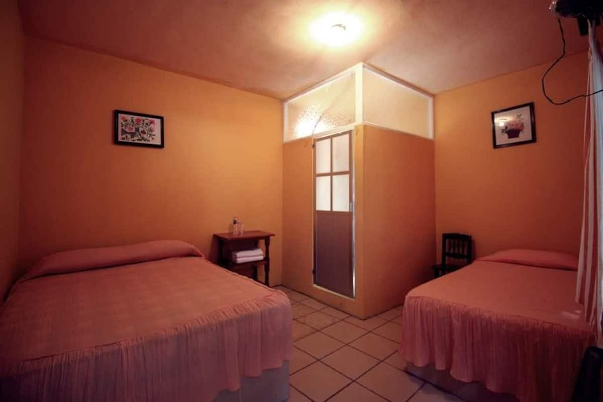 Quarto com duas camas, uma mesinha, janela com vista e luminária no teto.