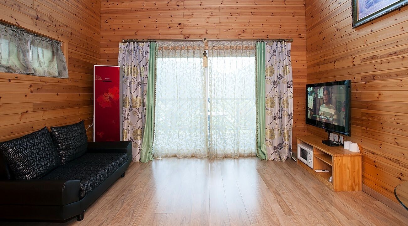 Um quarto com painéis de madeira, um sofá preto, uma televisão e um armário vermelho.
