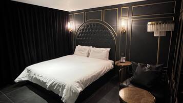 Quarto moderno com uma cama grande, uma mesinha lateral redonda, um banquinho redondo pequeno e uma luminária fixada na parede.