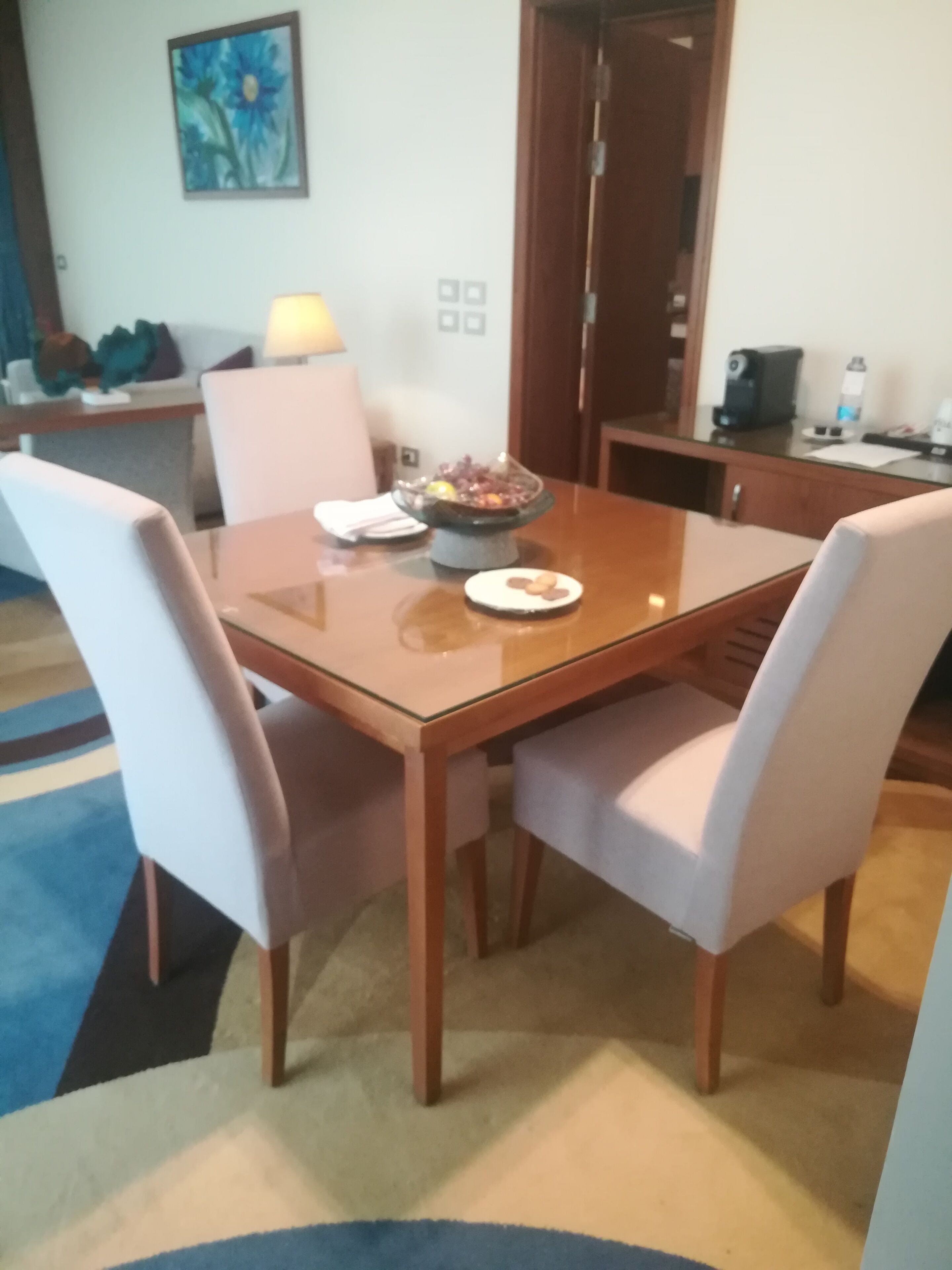 Uma área de refeições com mesa de madeira, quatro cadeiras, uma cesta de frutas e um abajur.