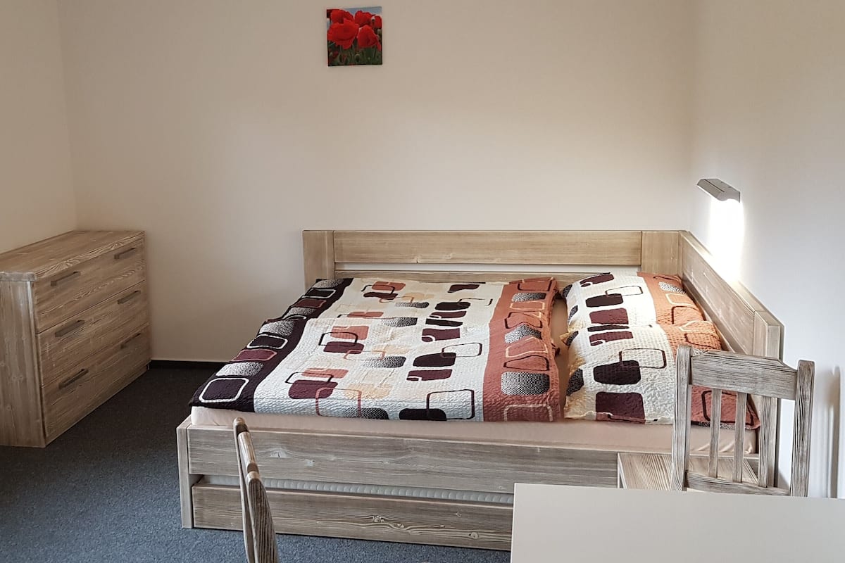 Quarto com cama de madeira, penteadeira de madeira e uma janela pequena.