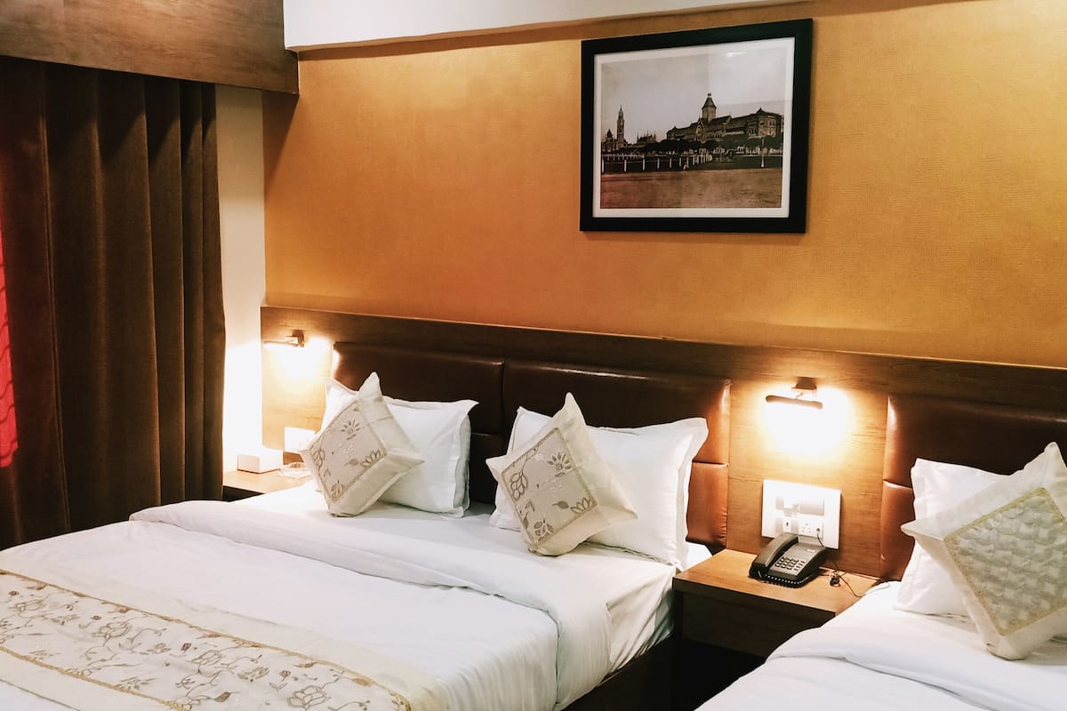 Quarto de hotel com duas camas, uma mesa de cabeceira com telefone e um quadro pendurado na parede.