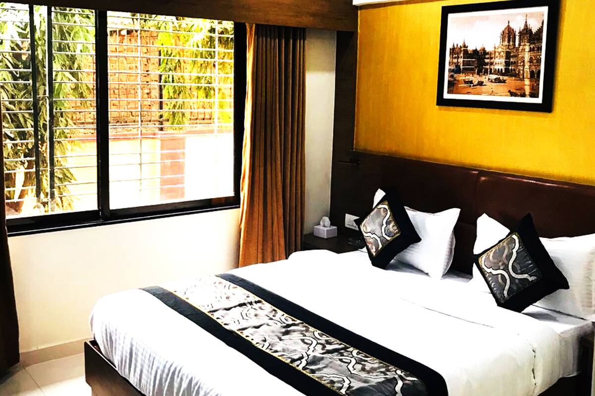 Quarto de hotel com uma cama grande, ar condicionado, ventoinha no teto, janela com cortinas e um quadro na parede.