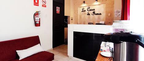 Uma área de recepção de hotel com um sofá vermelho, uma máquina de café e uma placa com a inscrição 'La Casa de Frima'.