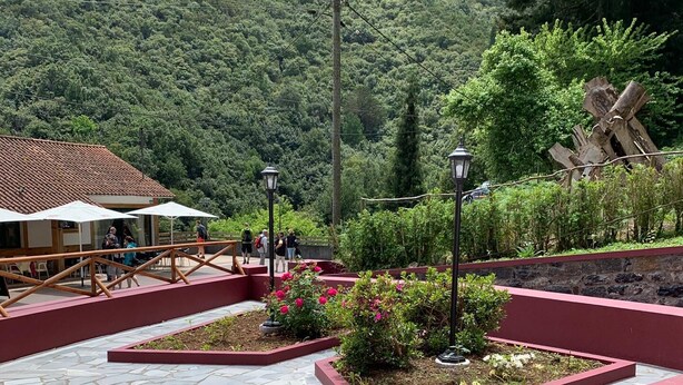 Pátio de pedra com mesas ao ar livre e vista para uma encosta arborizada.