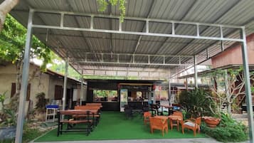 Um café ao ar livre com área de estar coberta, mesas e cadeiras.