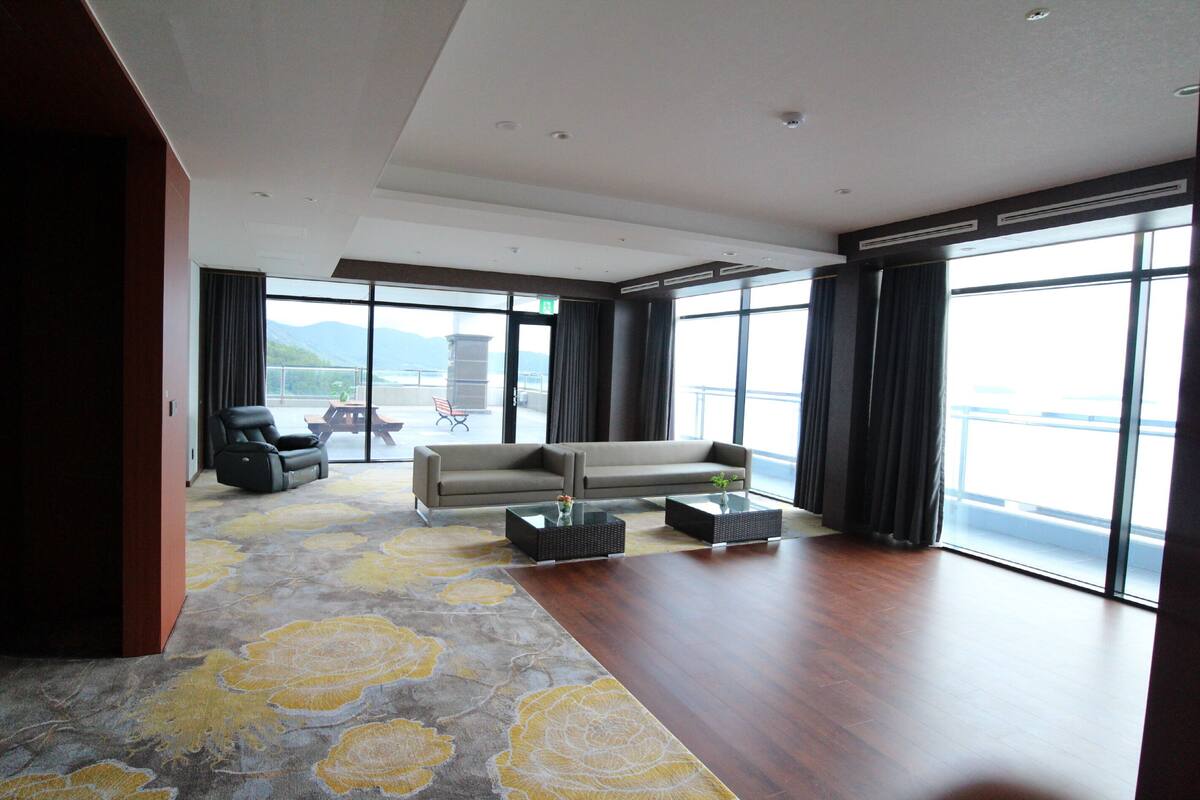 Quarto de hotel moderno com uma janela grande, um sofá, uma mesa de centro e uma cadeira.