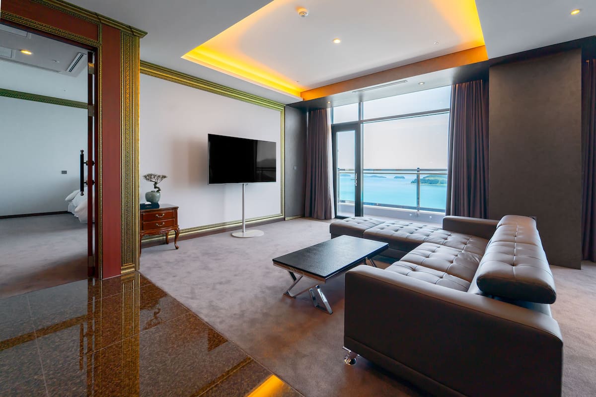 Quarto de hotel moderno com um sofá grande, uma TV de tela plana e vista para o mar.