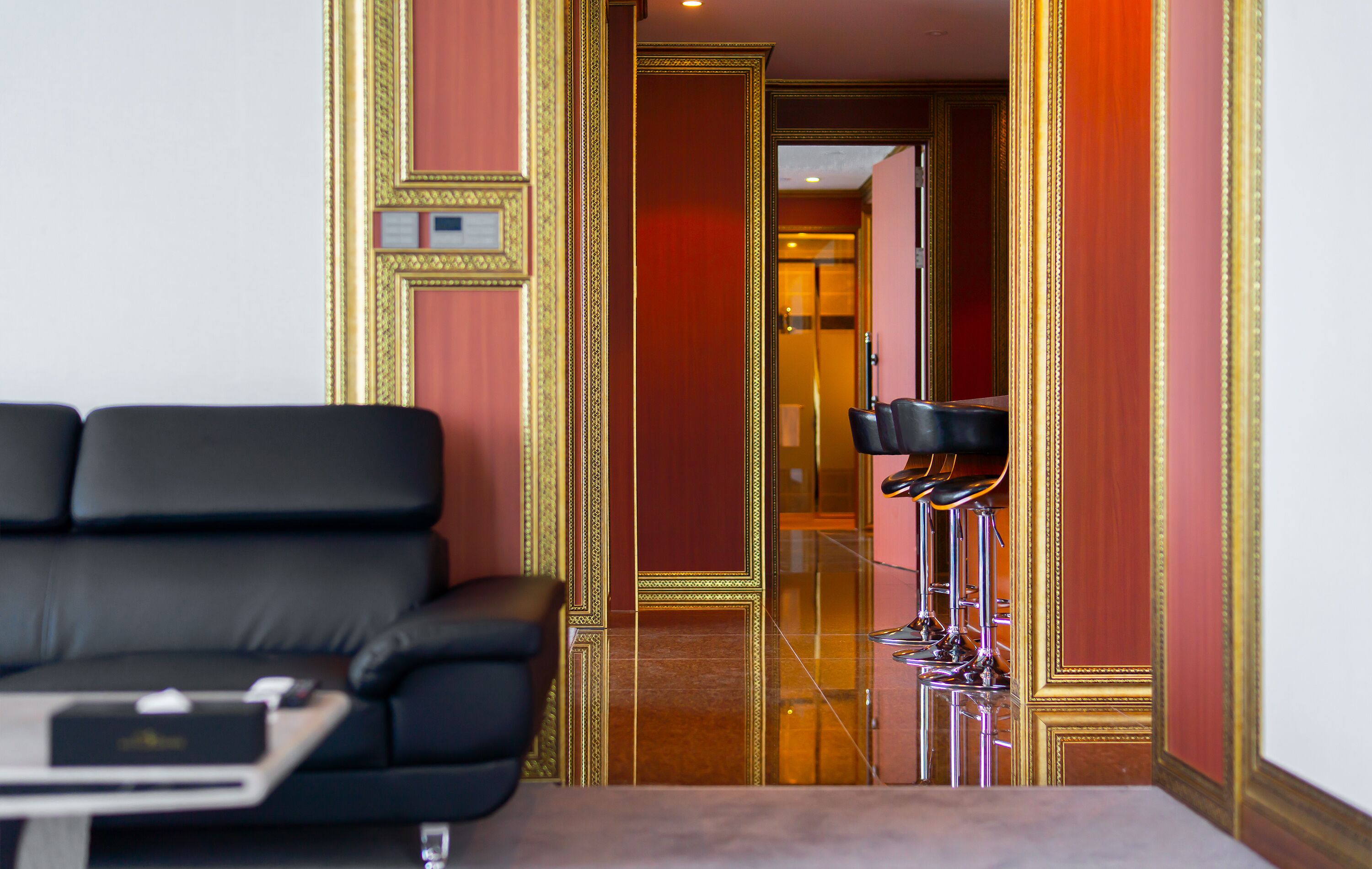 Um hall de hotel com um sofá de couro preto, uma mesinha com um tabuleiro e uma área de bar com banquetas.