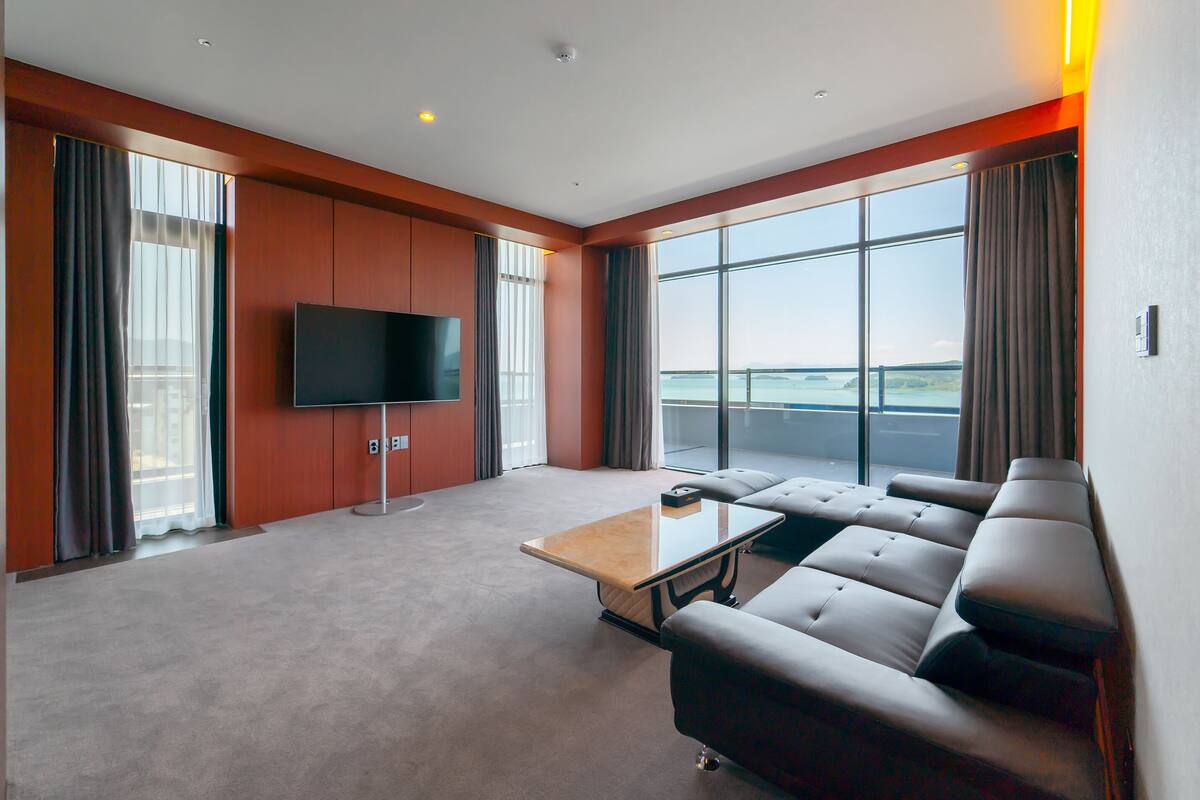 Quarto de hotel moderno com uma grande janela, uma TV de tela plana, um sofá e uma mesa de centro.