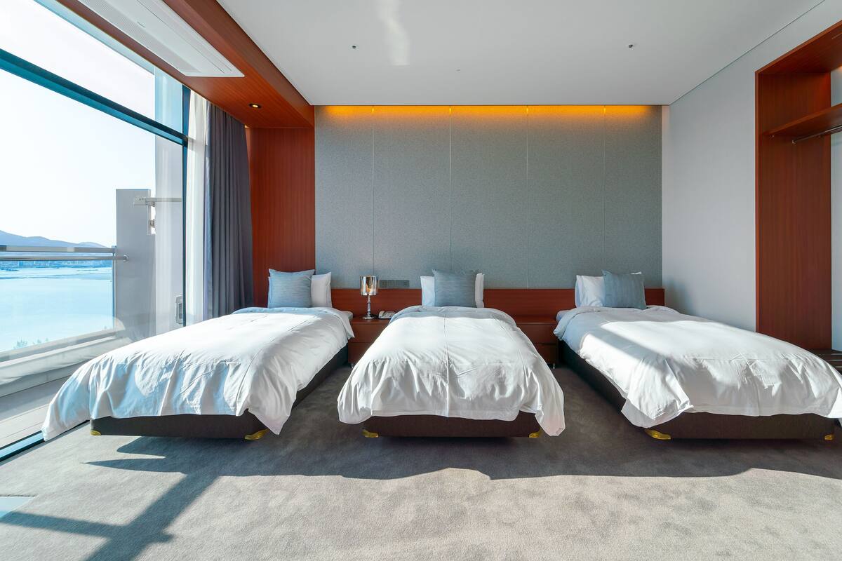 Quarto de hotel com duas camas, uma janela grande e vista para o mar.