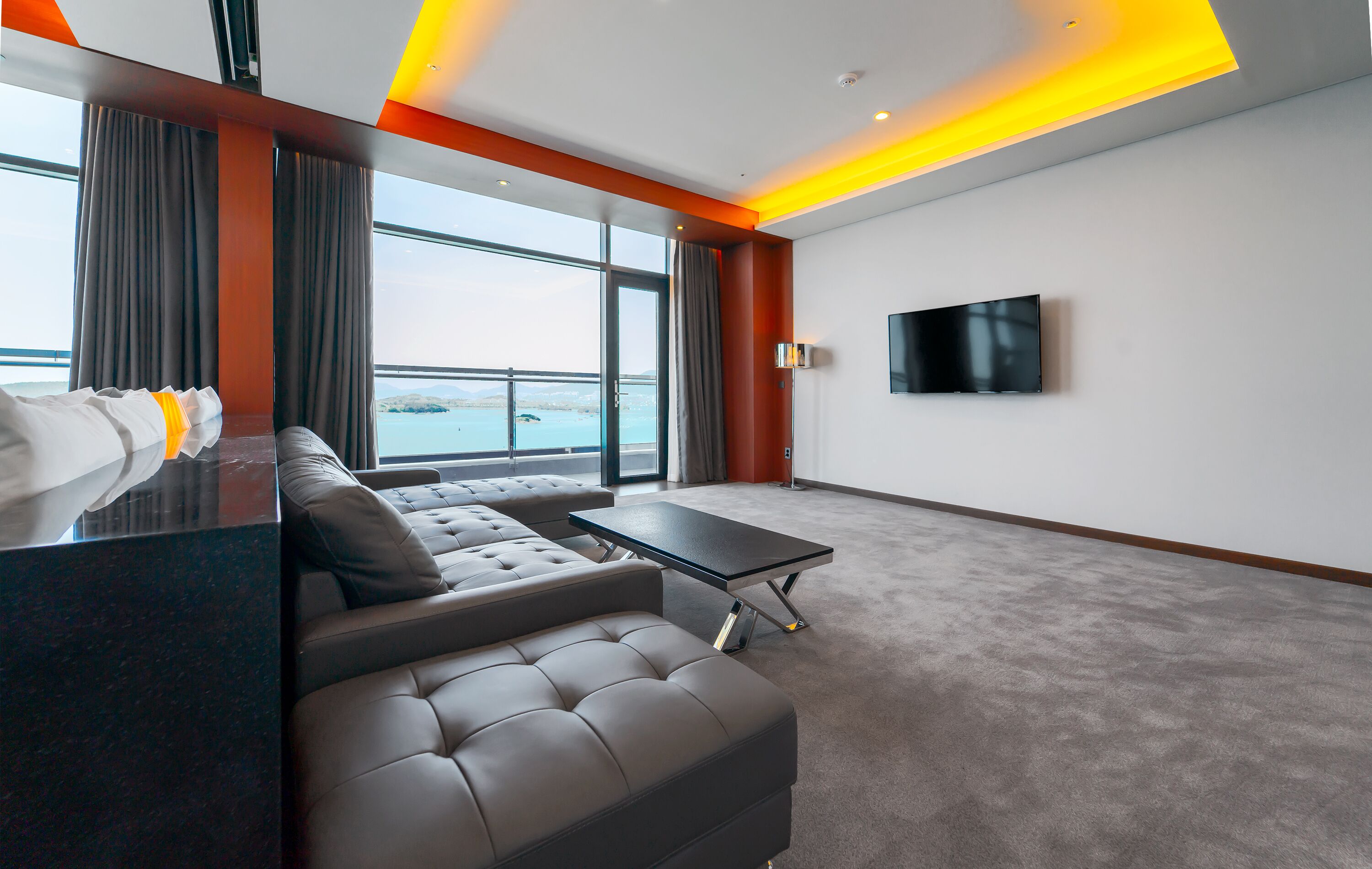 Sala moderna com um amplo sofá modular, uma televisão de tela plana e vista para o mar.