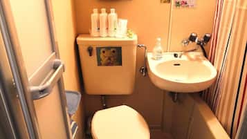Uma casa de banho compacta com sanita, lavatório e espelho pequeno. Há produtos de higiene no lavatório e uma toalha pendurada na parede.