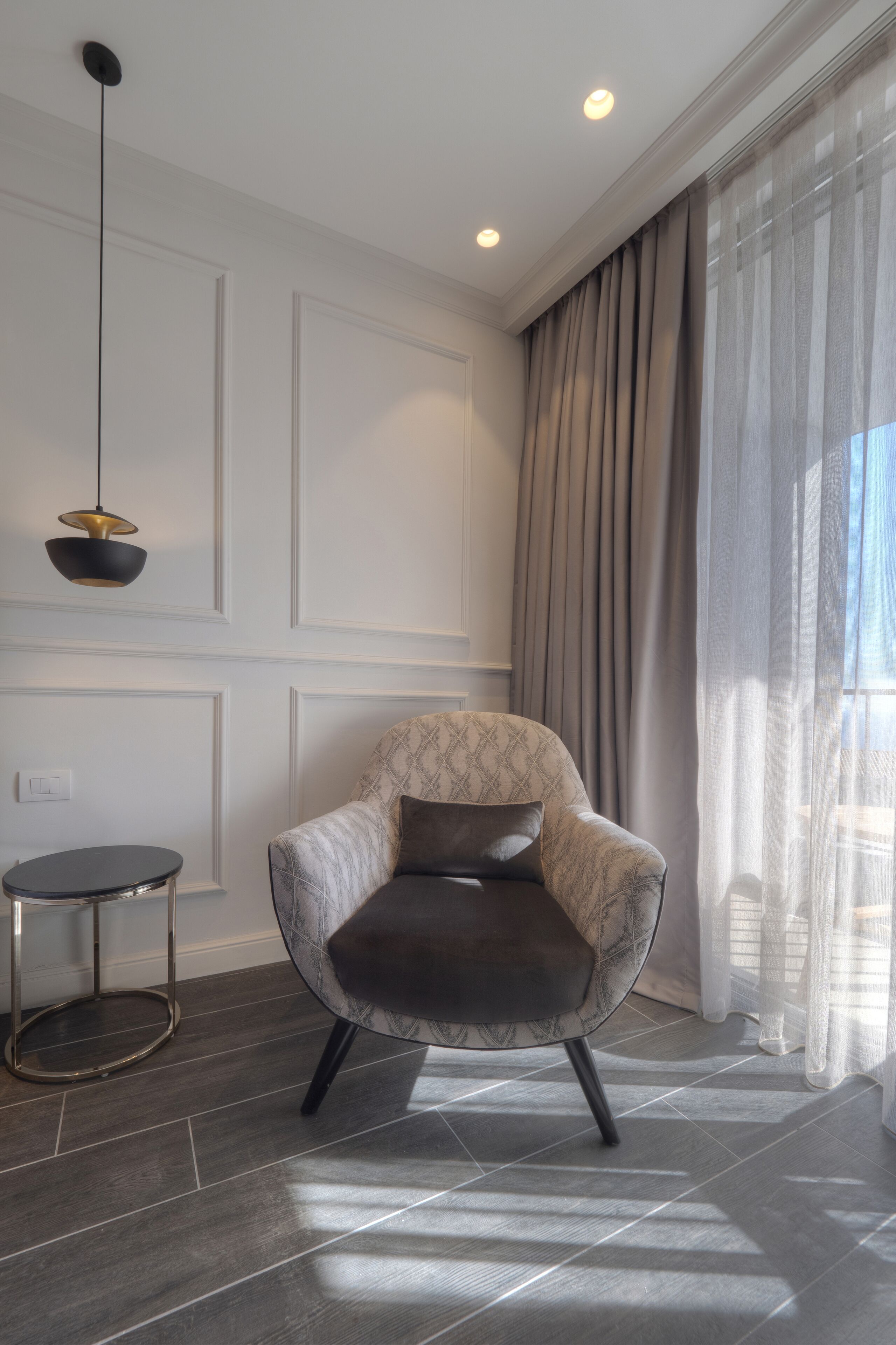 Uma sala de estar moderna com uma poltrona estampada, uma mesinha redonda e uma luminária pendente.