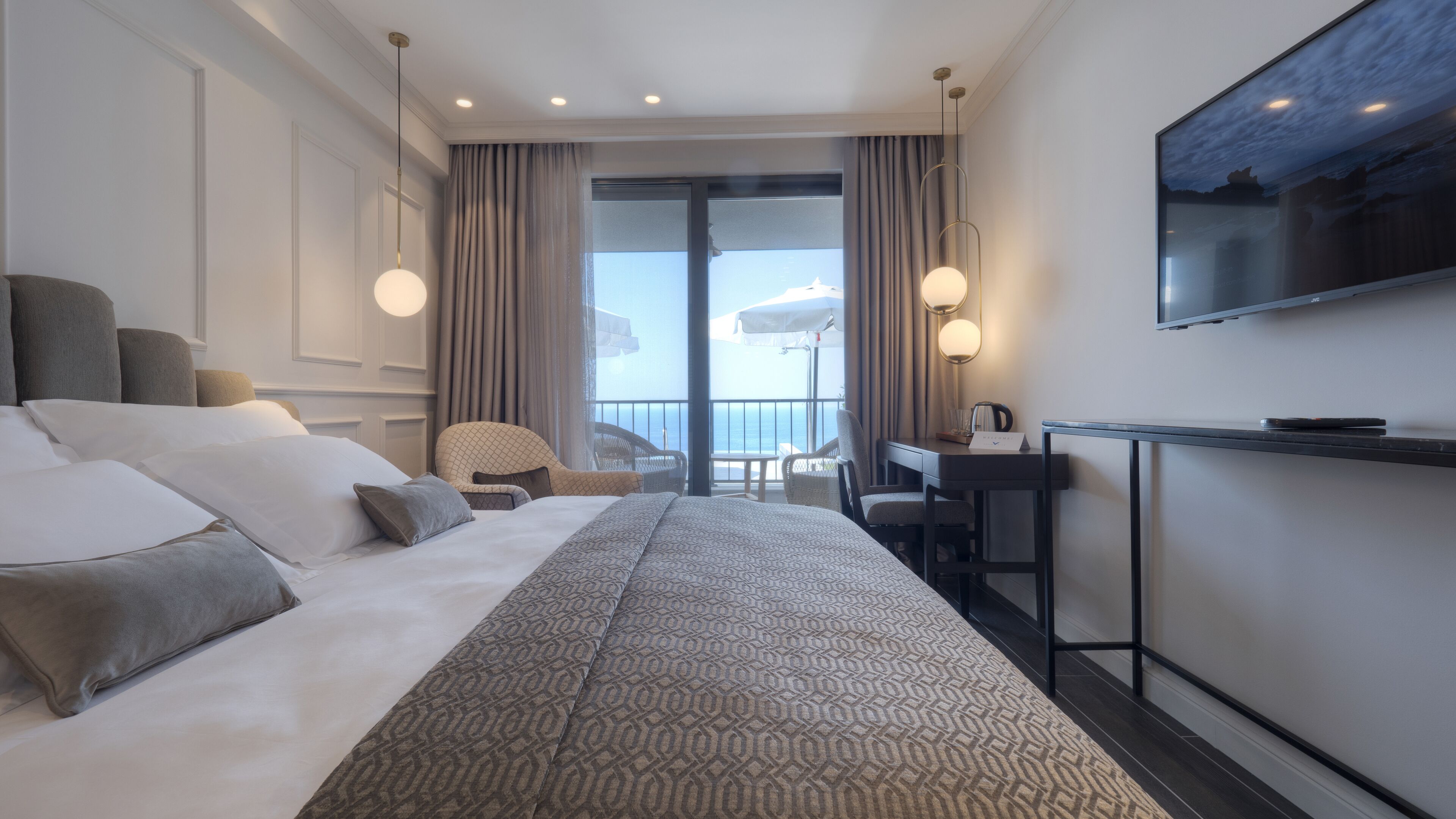 Quarto de hotel com uma cama grande, uma escrivaninha, uma cadeira, uma TV e uma varanda com vista para o mar.