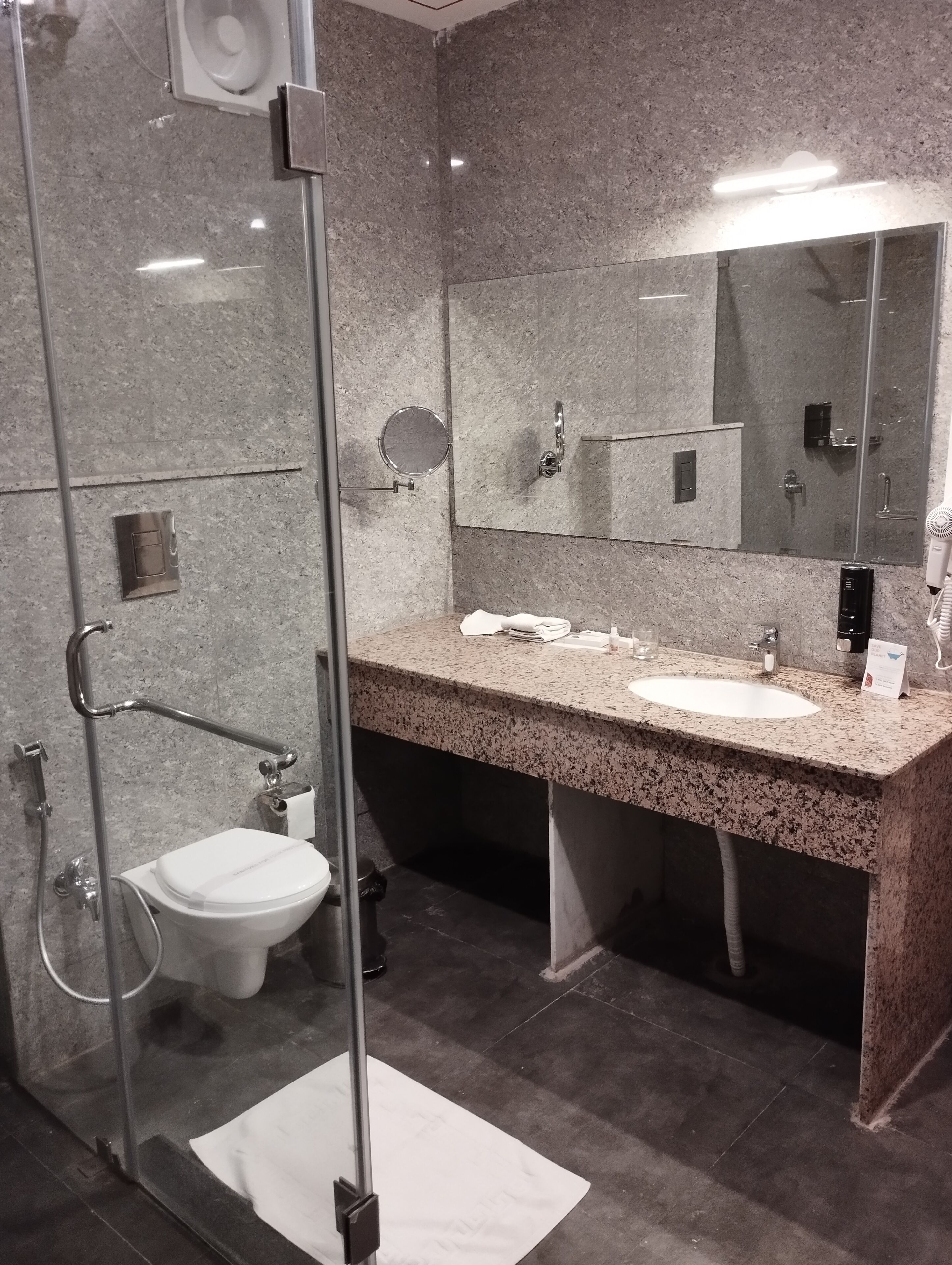 Uma casa de banho moderna com cabine de duche em vidro, sanita branca e bancada de granito com lavatório.