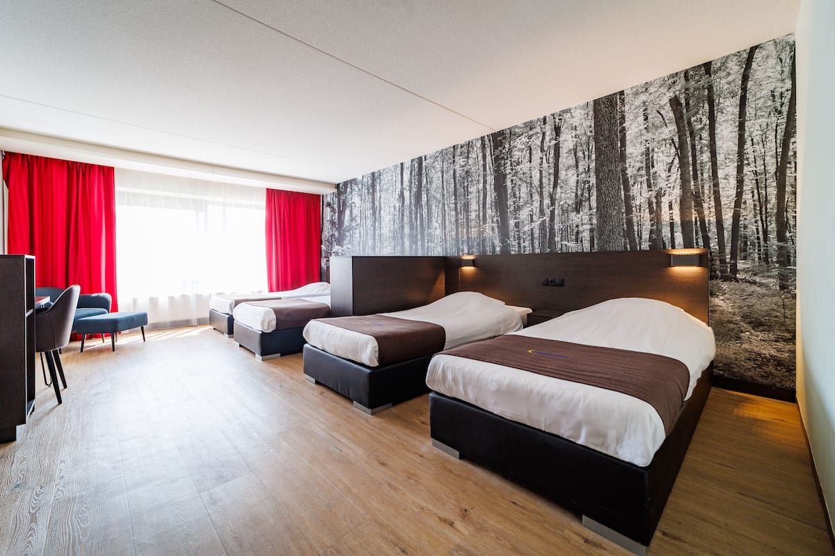 Quarto de hotel moderno com duas camas, uma escrivaninha e um grande mural com tema de floresta.