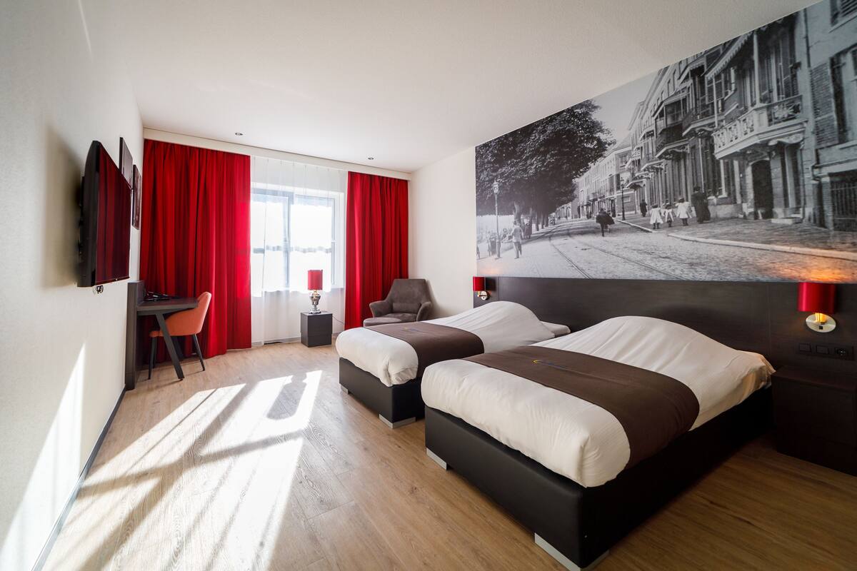 Quarto de hotel com duas camas, uma escrivaninha e uma cadeira.