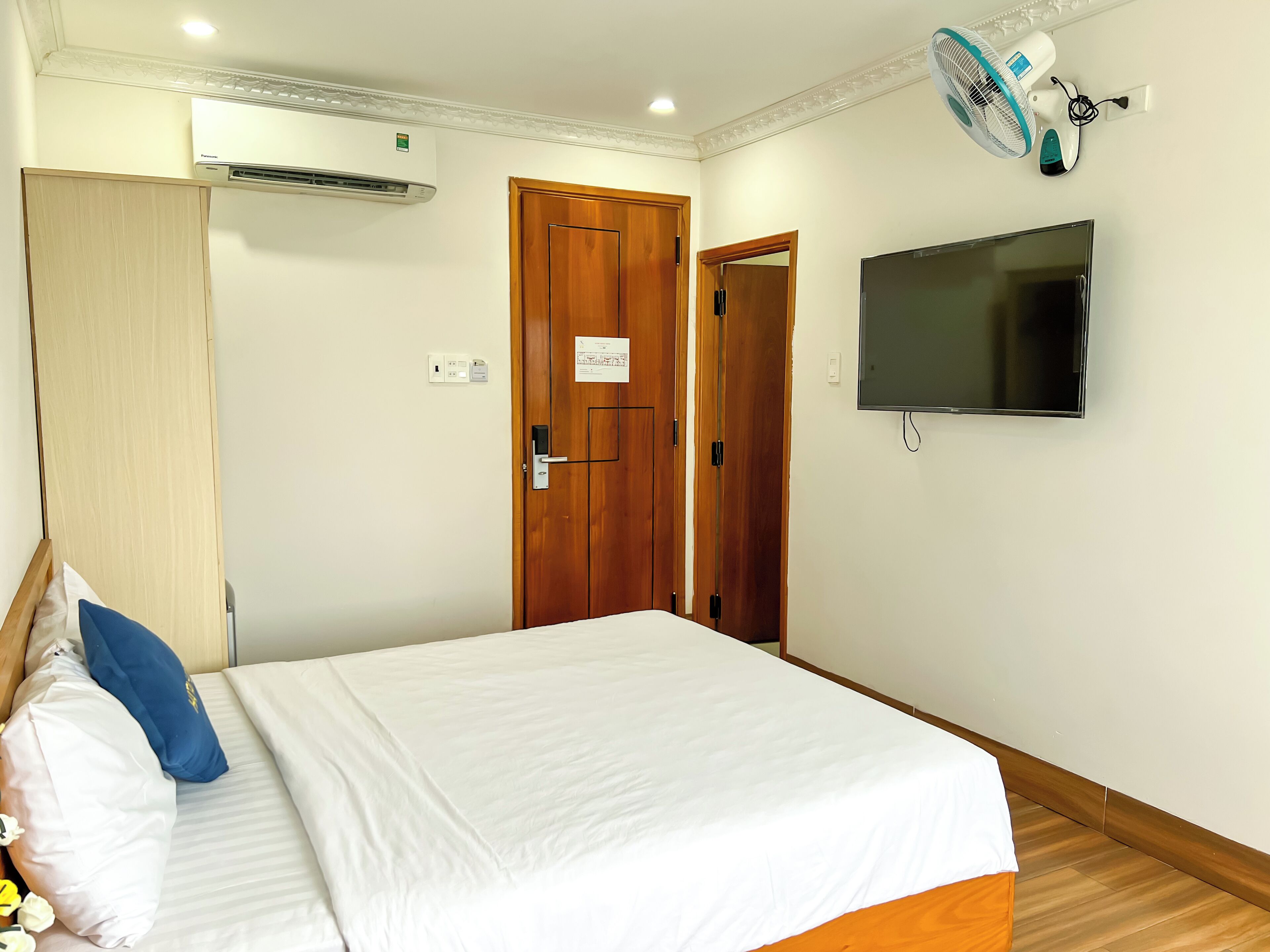 Quarto de hotel com cama, televisão, ar condicionado e porta de madeira.