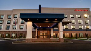Entrada de um hotel Hampton Inn com galeria coberta, fachada de tijolos e céu limpo.