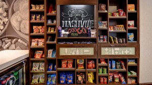 Exposição de petiscos com vários snacks e salgadinhos, um letreiro de boas-vindas e vista da cidade.
