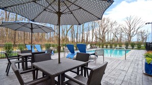 Uma área de pátio com móveis de vime, piscina e vista para árvores.